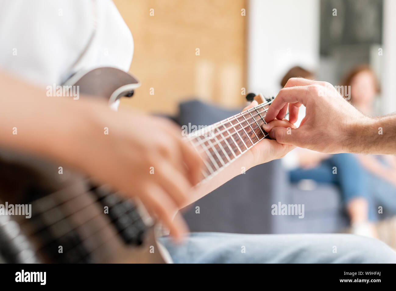 Young boy moves his hand along guitar strings while his father helps ...