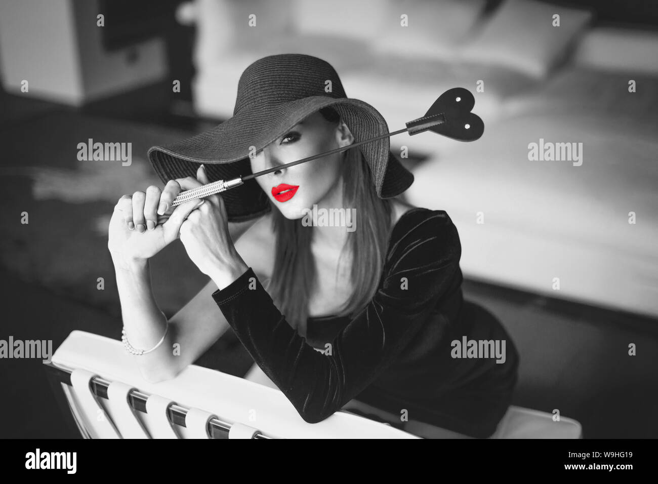 Passionate dominant femme fatale in hat holding whip in front of face ...