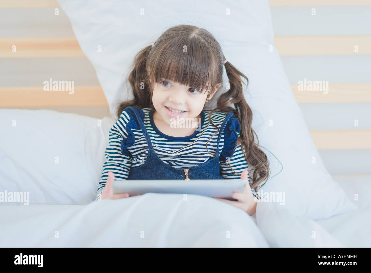 Cute kid girl smiling while using digital smart tablet on bed in kid's ...