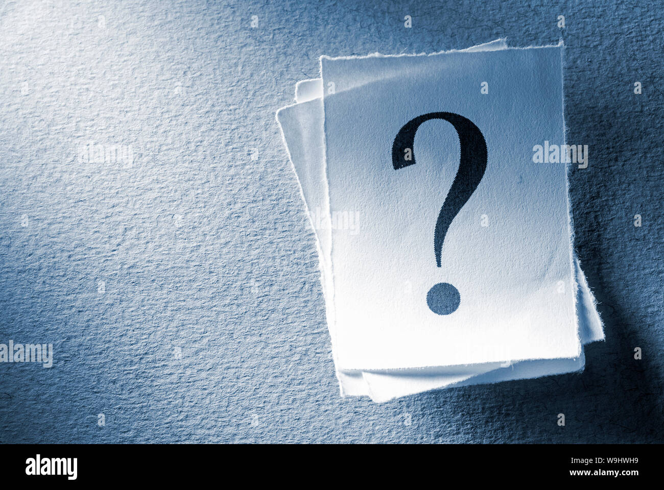Pile of printed question marks in shaft of light on a textured grey ...
