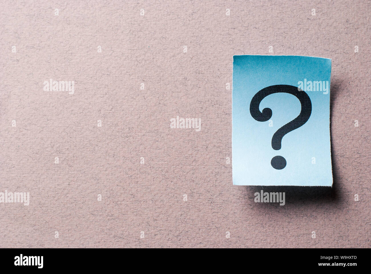 Printed question mark on curled blue paper over a grey background with ...