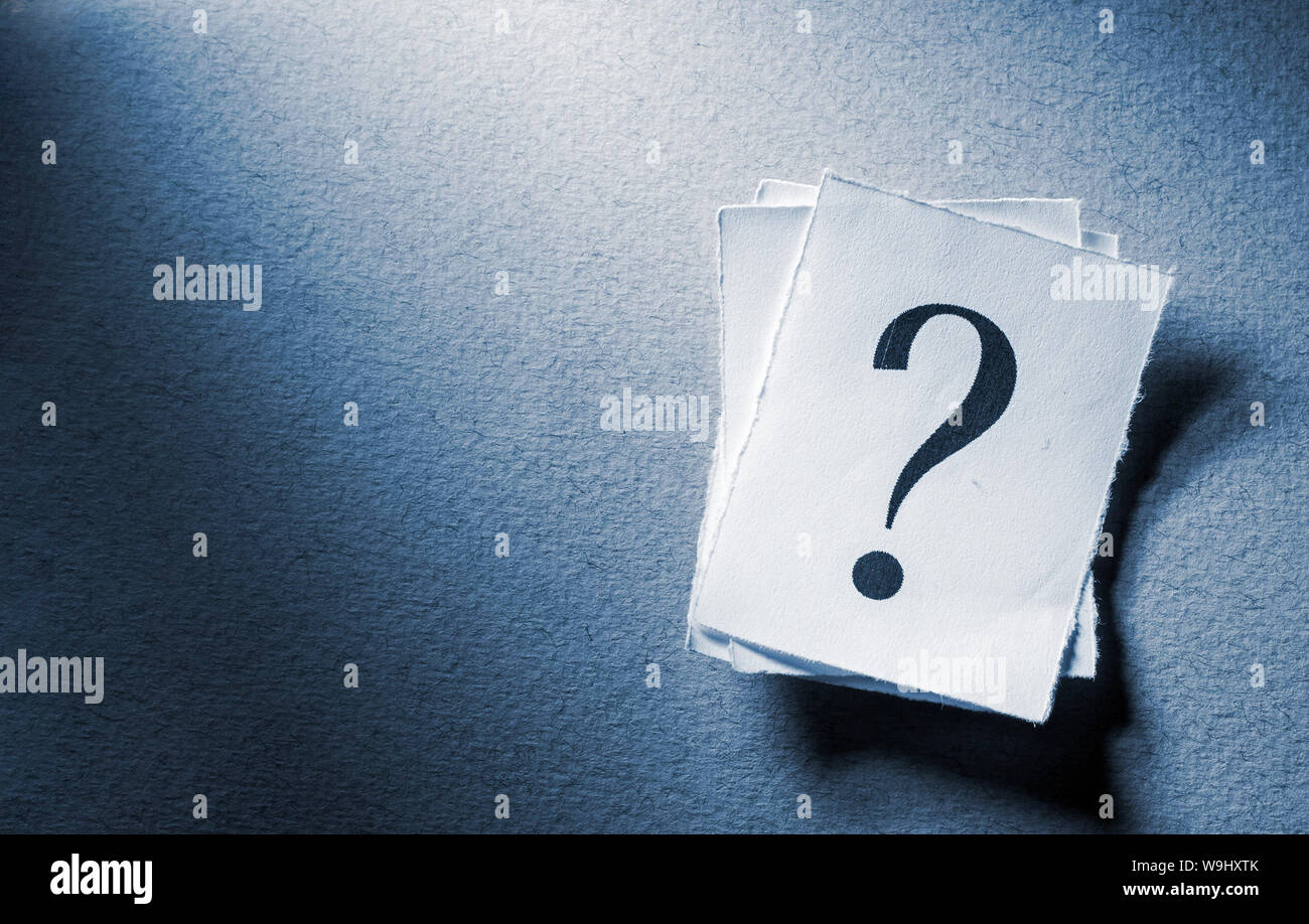 Pile of printed question marks in shaft of light on a textured grey ...