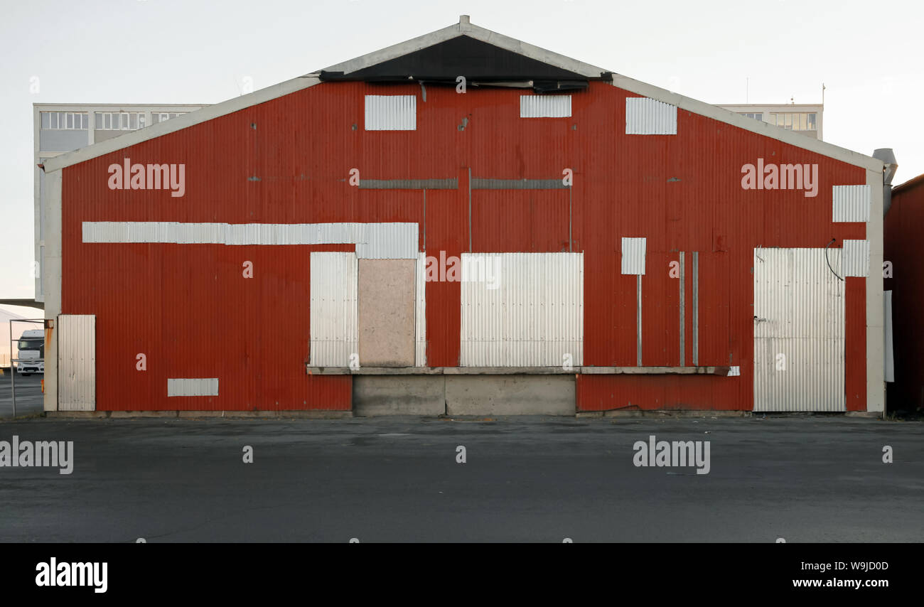 Red warehouse wall with closed gray gates Stock Photo - Alamy