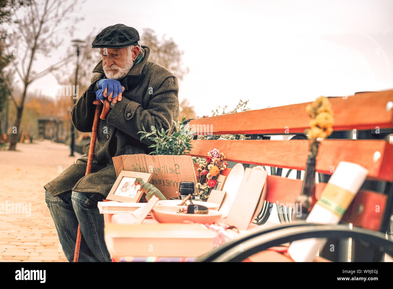 Side view of a sad poor man sitting on bench selling stuff Stock Photo ...