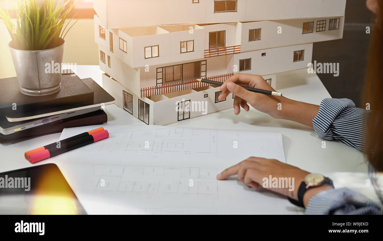 Female architect working with model house and blueprint in home office ...