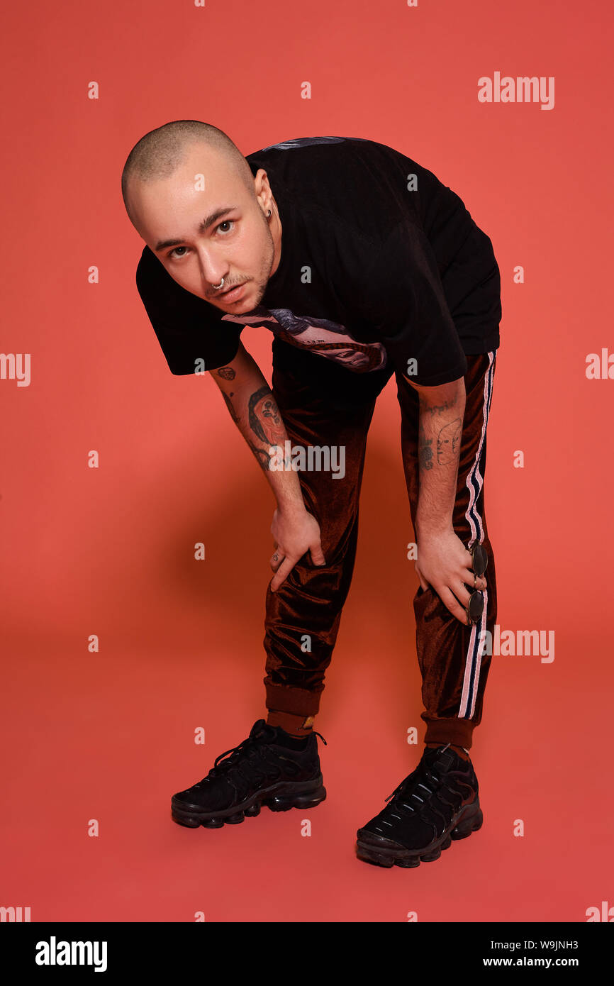 Studio shot of a young tattoed bald man posing against a pink ...