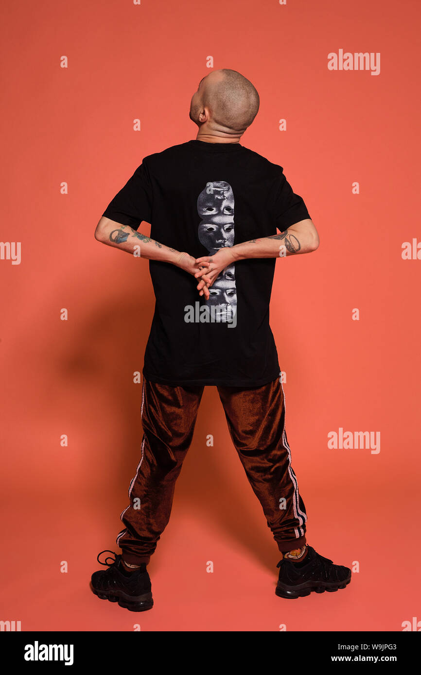 Studio shot of a young tattoed bald man posing against a pink ...