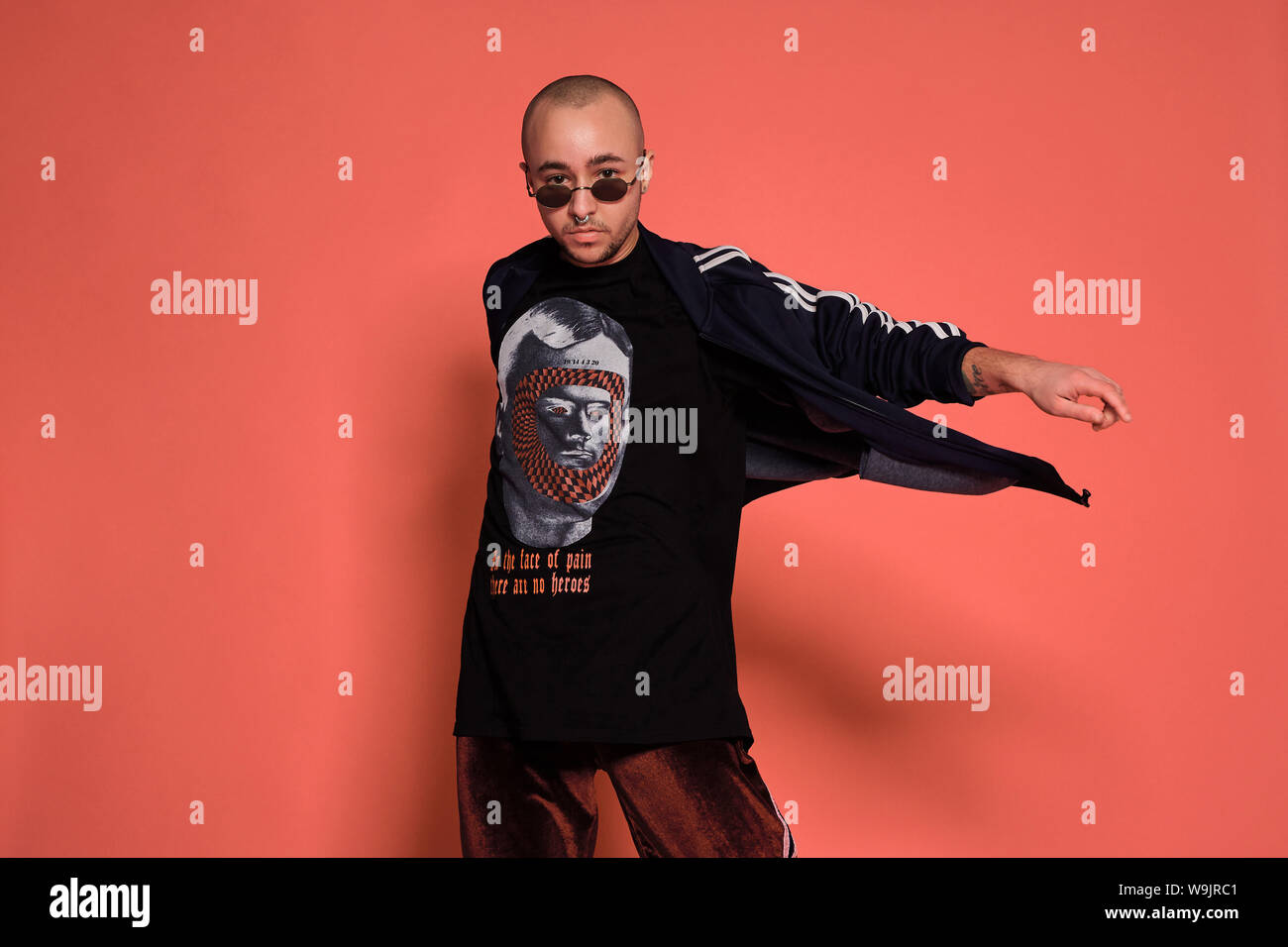 Studio shot of a young tattoed bald man posing against a pink ...