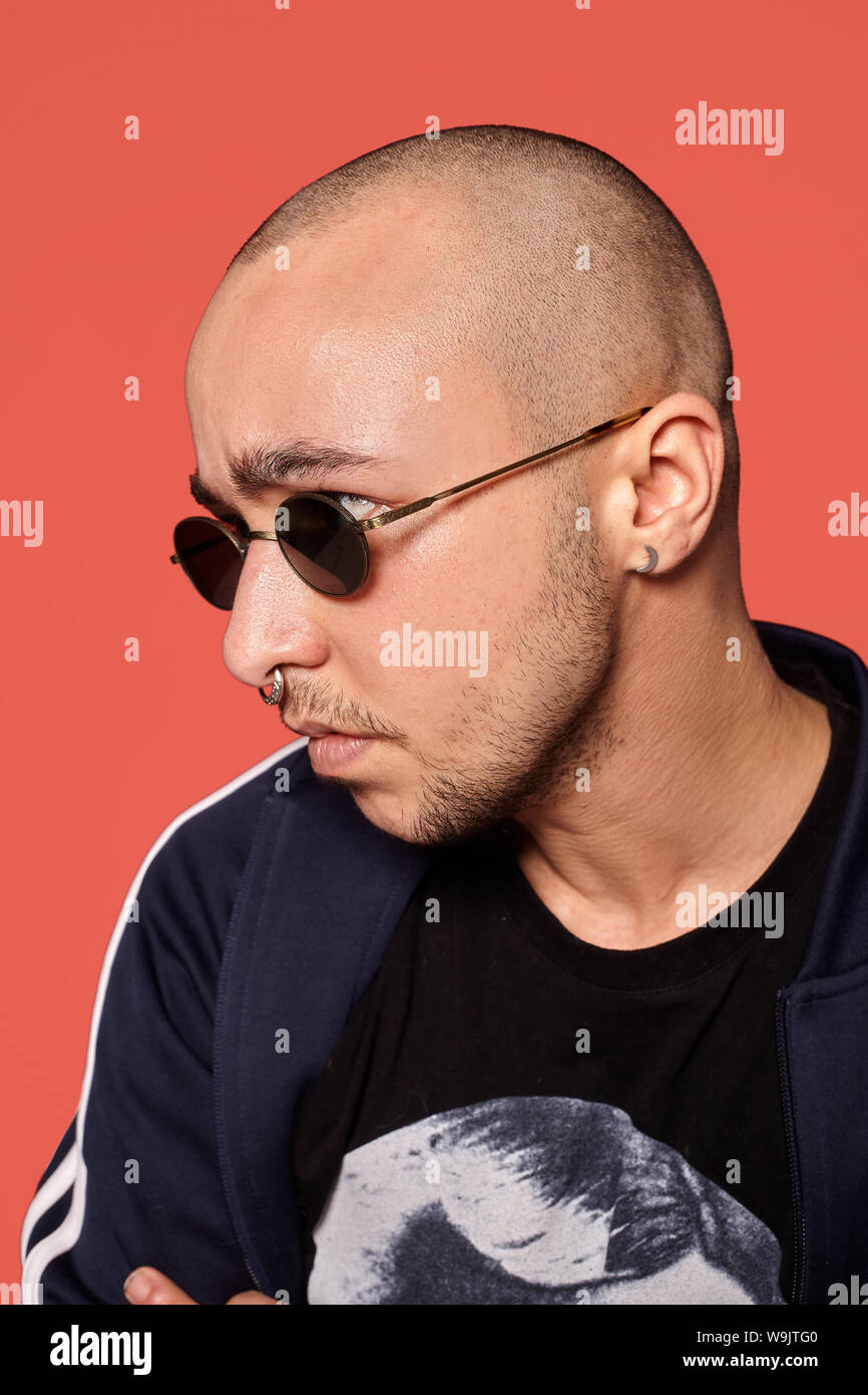 Studio shot of a young tattoed bald man posing against a pink ...