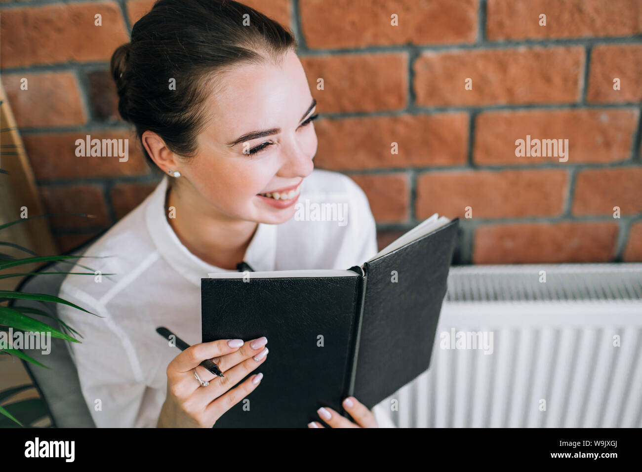 Happy young woman laughing, holding black notepad and a pen on a brick ...