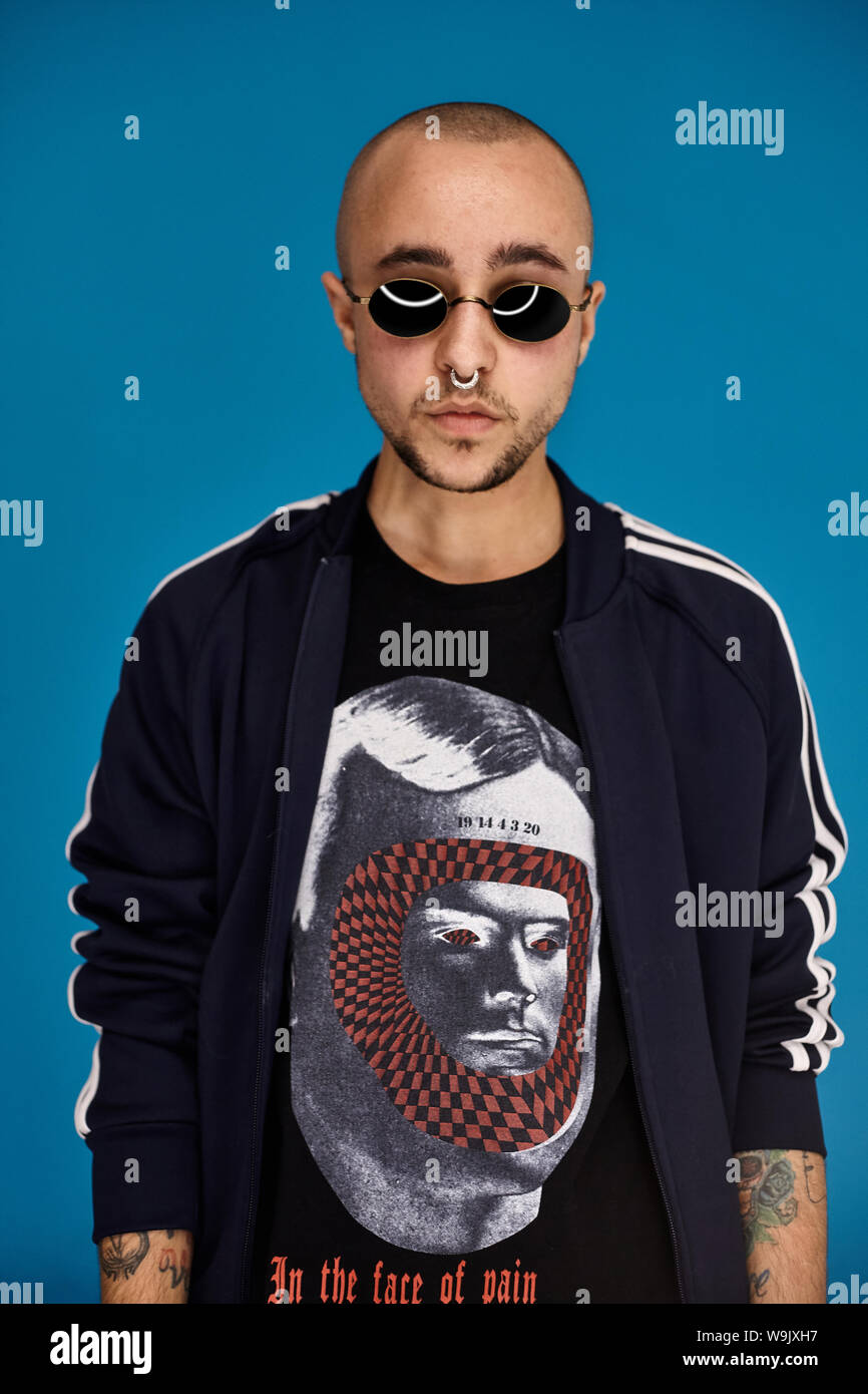 Studio shot of a young tattoed bald man posing against a blue ...