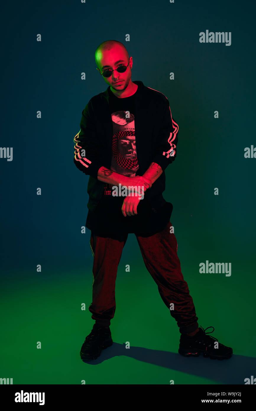 Studio shot of a young tattoed bald man posing against a colorful ...