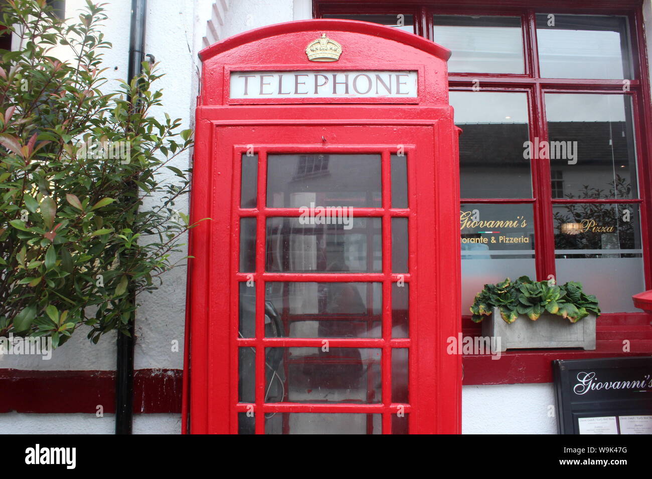 Image of a red telephone box in front of white building with leaves ...