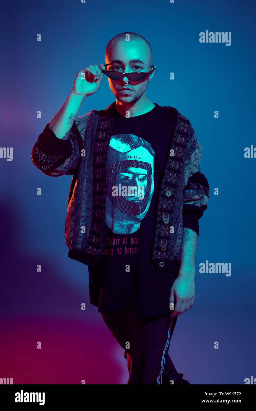 Studio shot of a young tattoed bald man posing against a colorful ...
