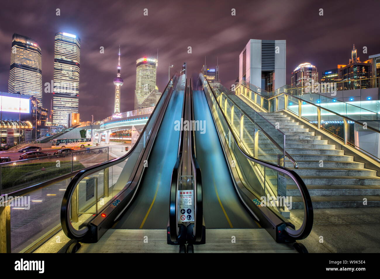 A modern, open-air escalator with Pudong cityscape at night, Shanghai ...
