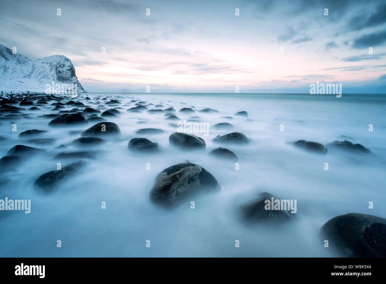 Rocks in the cold sea and snow capped mountains under the blue light of ...