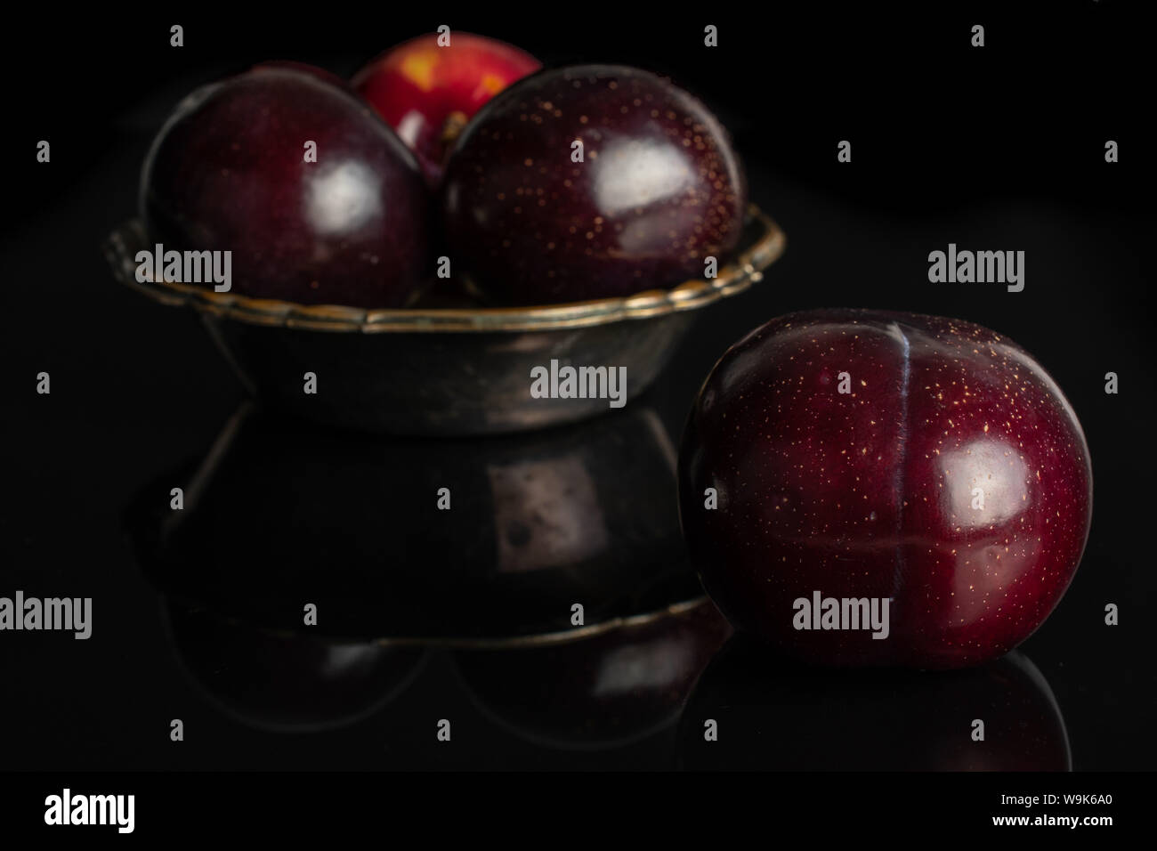 Group of four whole ripe red round plum in dark ceramic bowl isolated ...