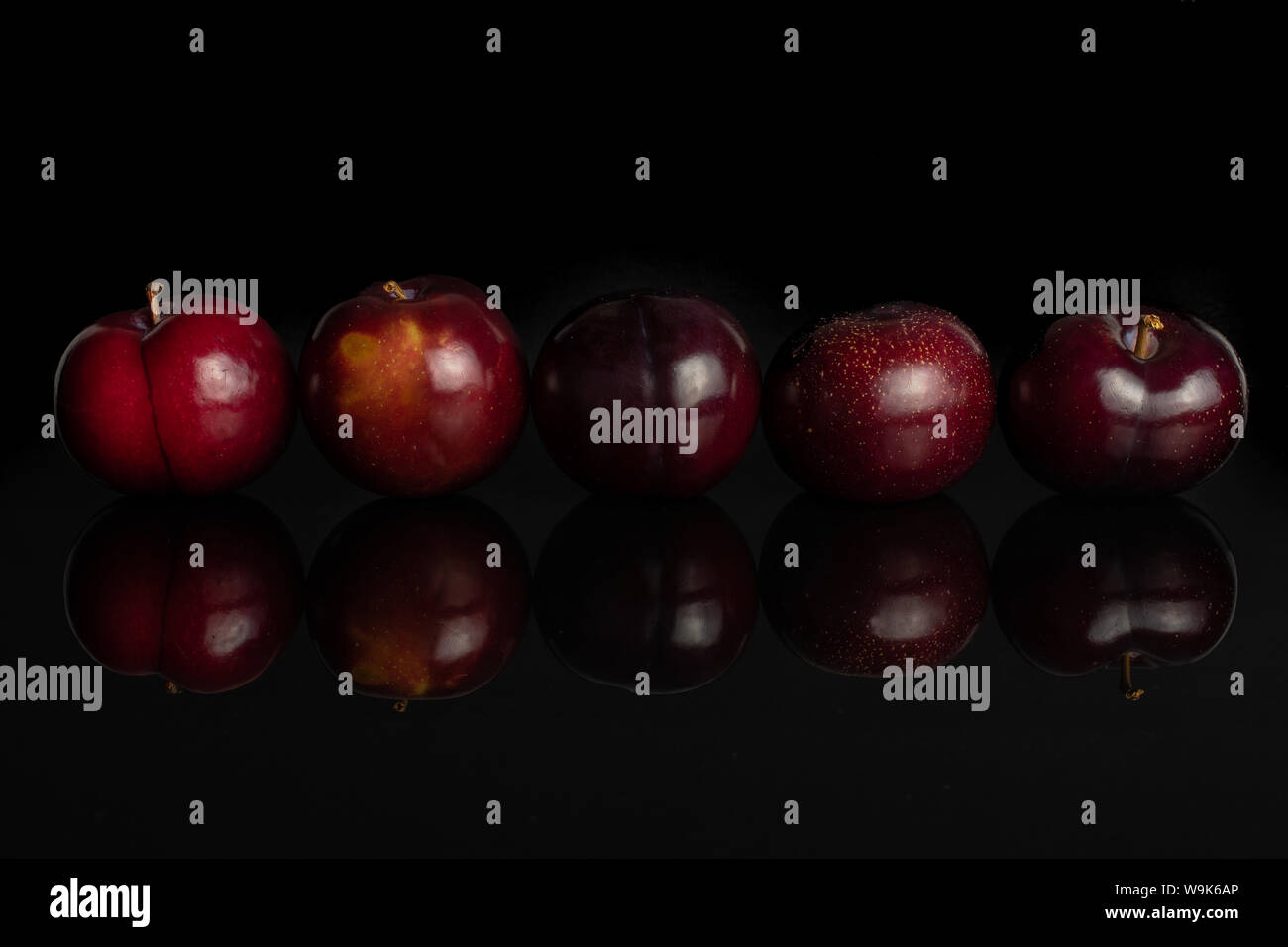 Group of five whole ripe red round plum in row isolated on black glass ...