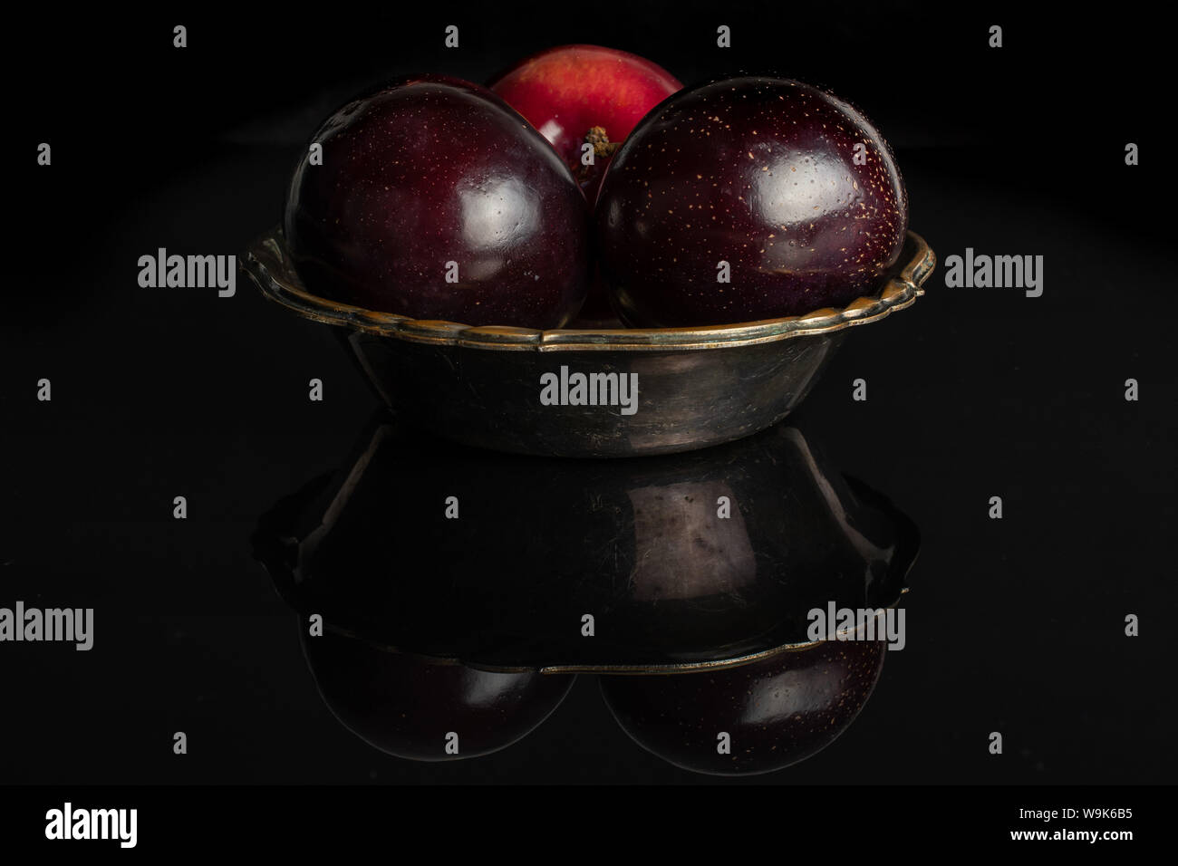 Group of three whole ripe red round plum in dark ceramic bowl isolated ...