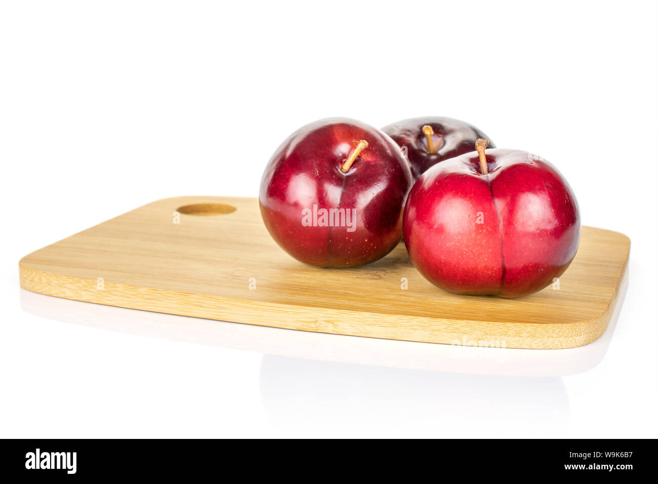Group of three whole ripe red round plum on bamboo cutting board ...