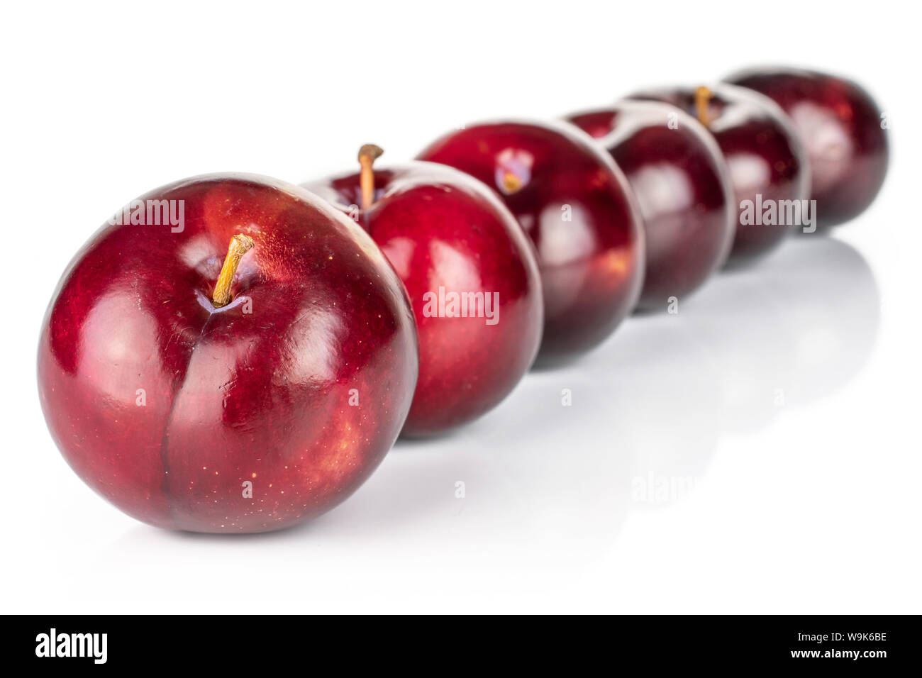 Group of six whole ripe red round plum placed diagonally in line ...