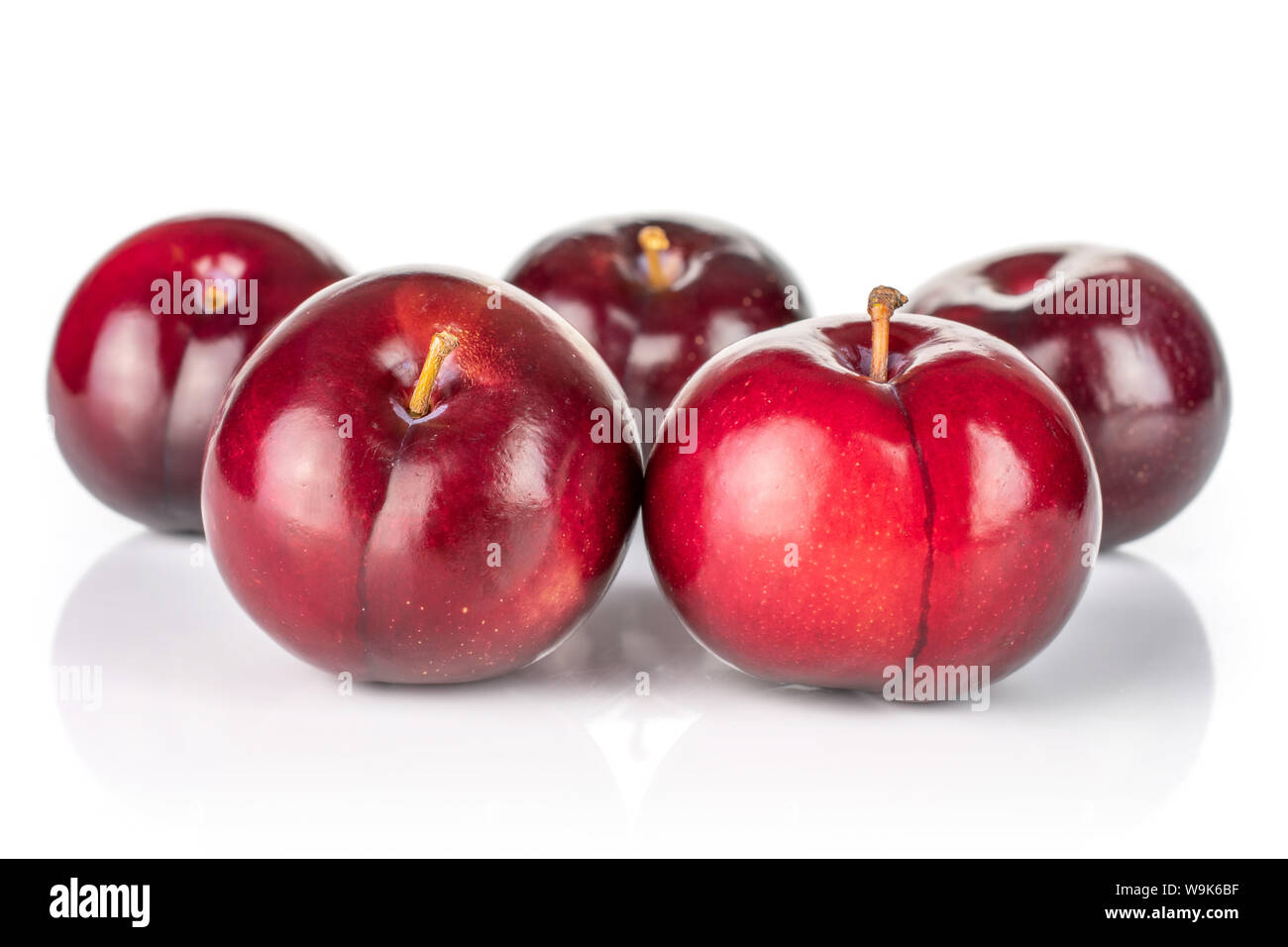Group of five whole ripe red round plum two are in the front arranged ...