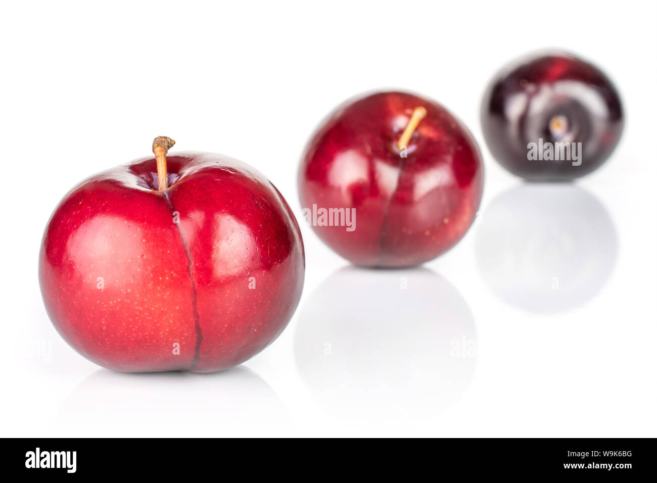 Group of three whole ripe red round plum placed diagonally in line ...