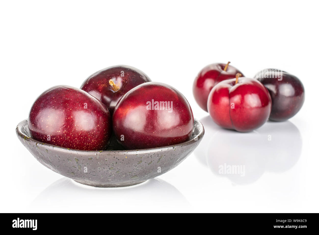 Group of six whole ripe red round plum in dark ceramic bowl isolated on ...