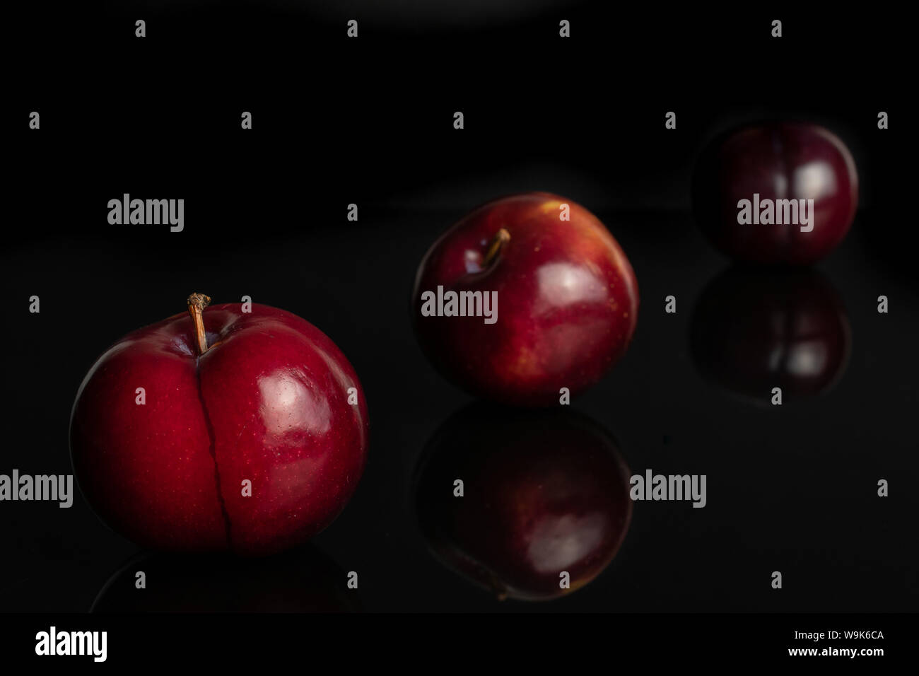 Group of three whole ripe red round plum placed diagonally in line ...