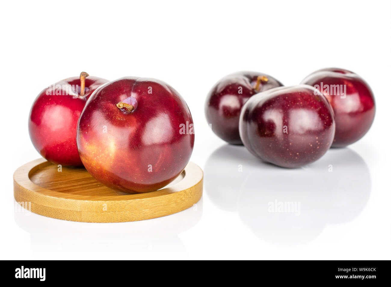 Group of five whole ripe red round plum on round bamboo coaster ...