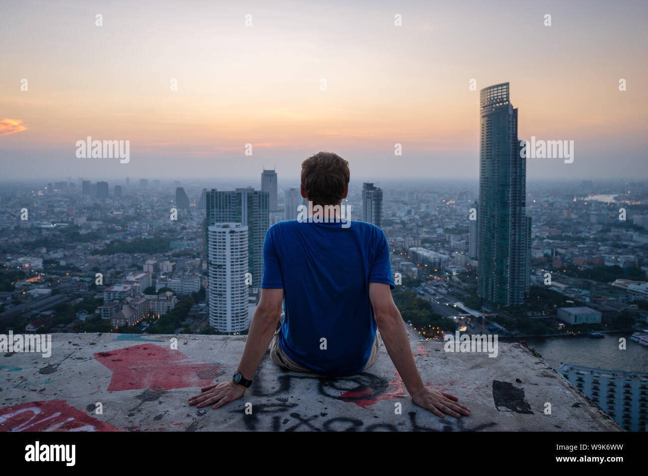 A single man watching sun set over city skyline at dusk, Bangkok ...