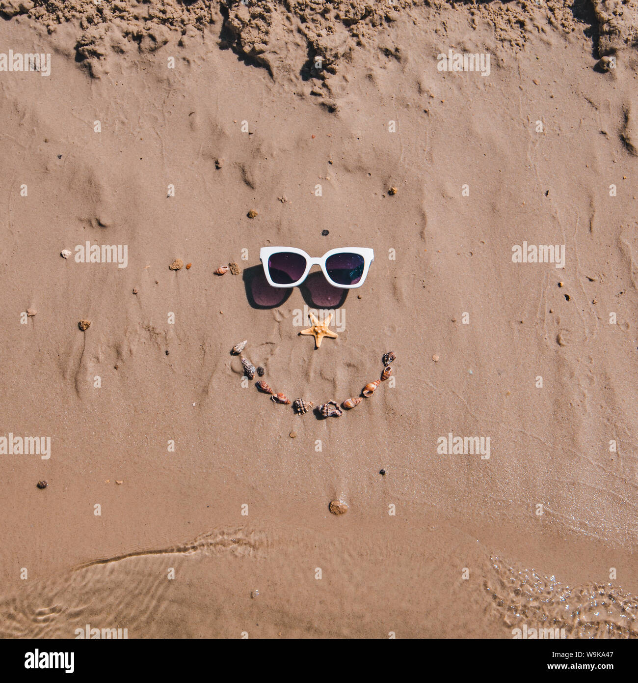 smile face drawn on sand with shells and sunglasses overhead top view ...