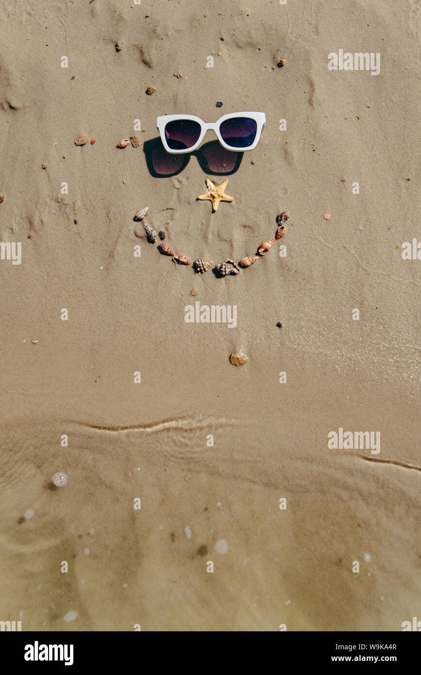 smile face drawn on sand with shells and sunglasses overhead top view ...
