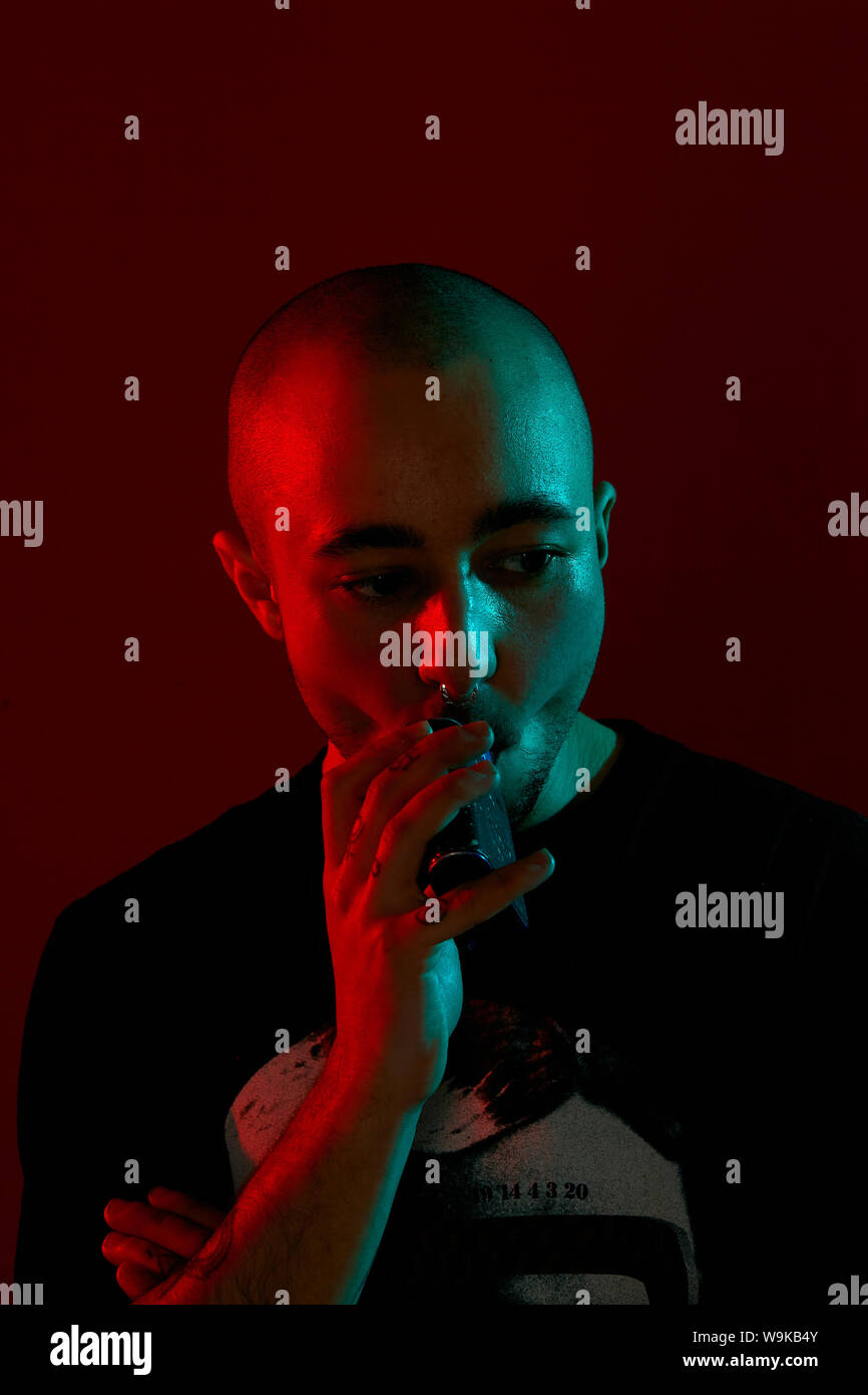 Close-up studio shot of a young bald guy vaping, blowing out a cloud of ...
