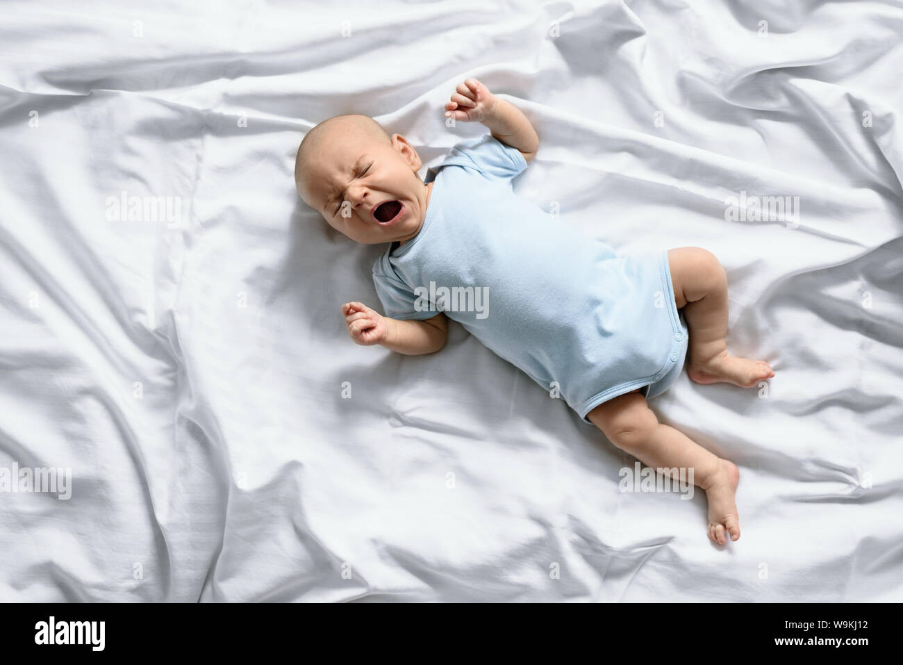 Top view portrait of newborn baby in blue bodysuit lying in white bed ...