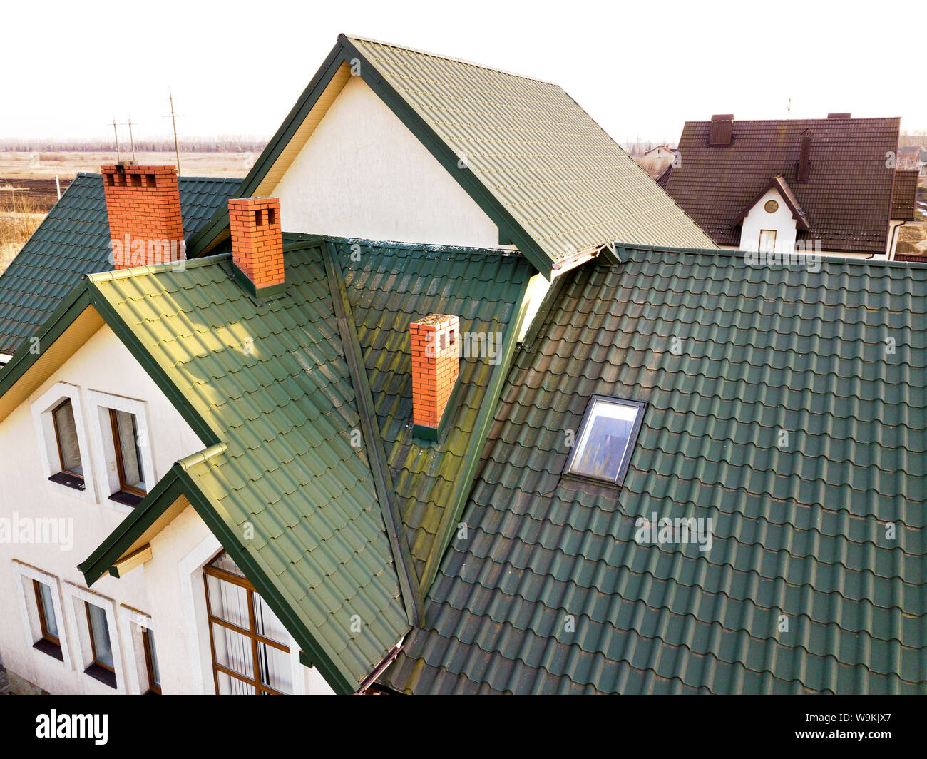 Green metal shingled house roof with attic plastic window and brick ...