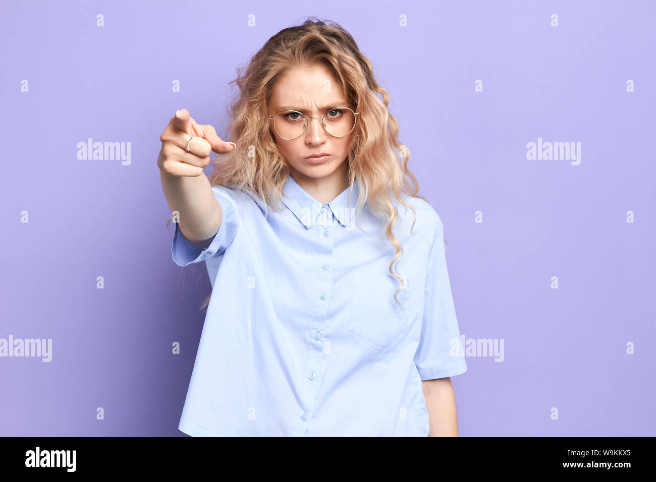 angry frustrated young woman pointing at camera over blue background ...