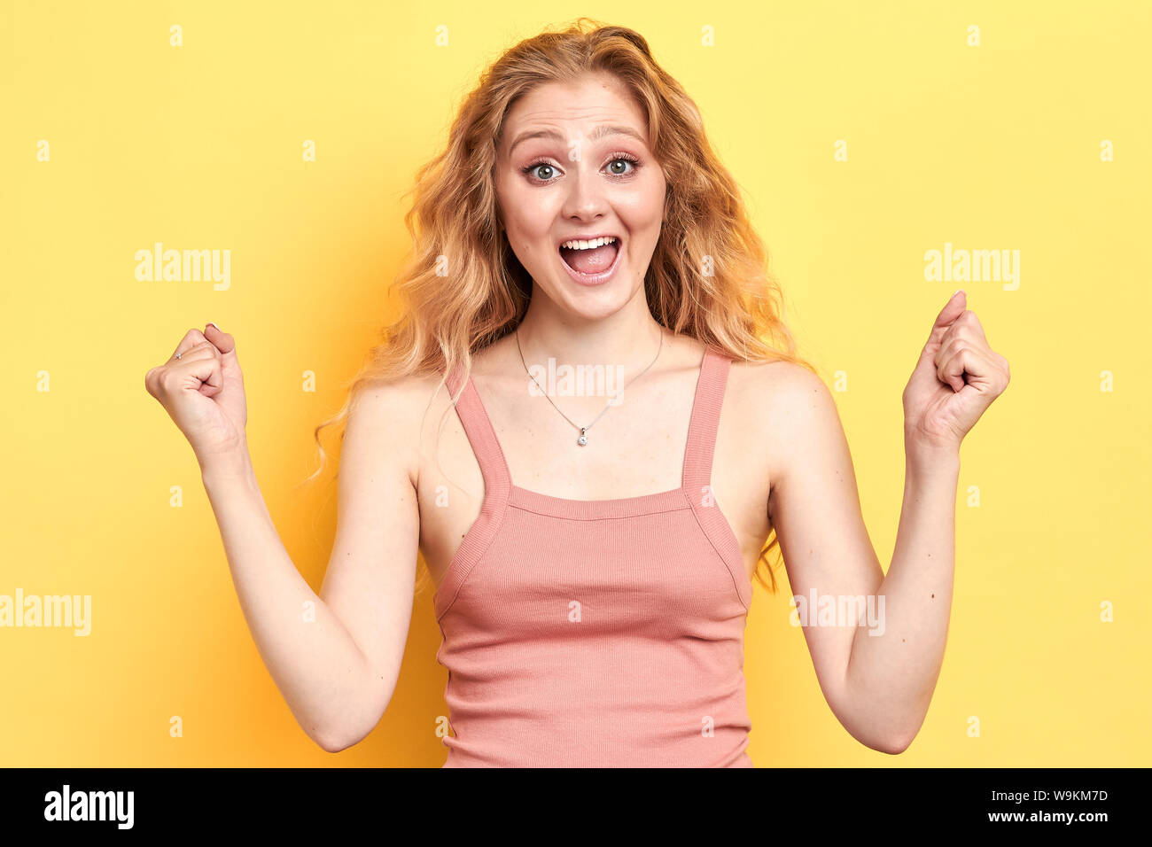 positive cheerful woman celebrating her success over yellow background ...