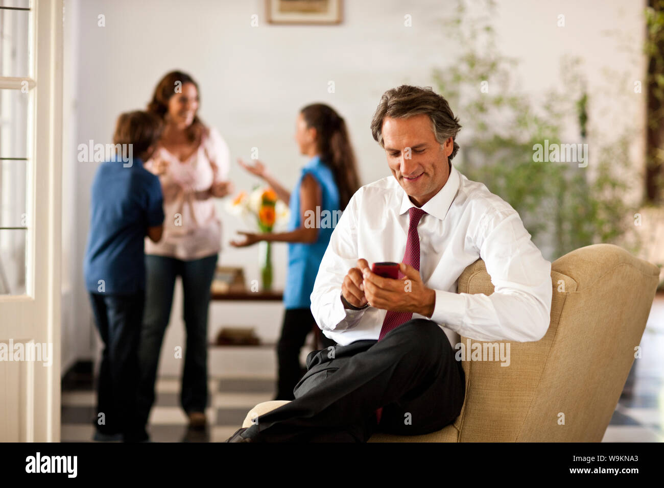 Man texting at home, with his family in the background Stock Photo - Alamy