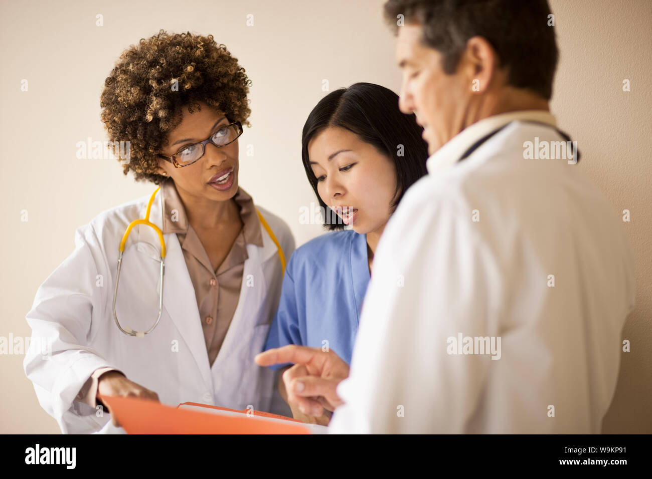Three doctors discussing patient files in a corridor Stock Photo - Alamy