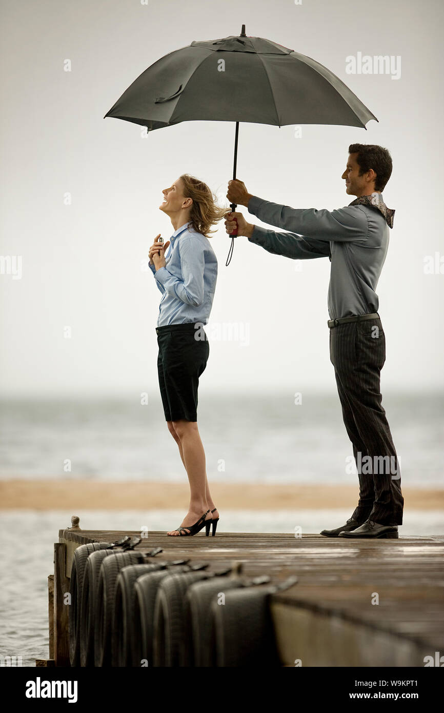 Mid-adult businessman shielding his business partner with umbrella ...