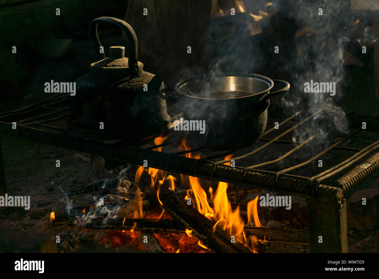a pot and a kettle stand over a fire on a portable hearth made of metal ...