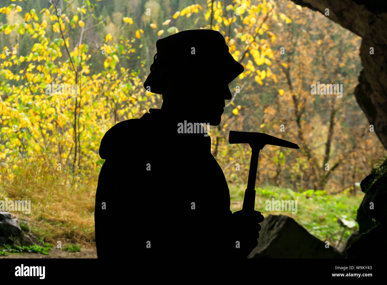 silhouette of a geologist with a geological hammer in a cave, on the ...
