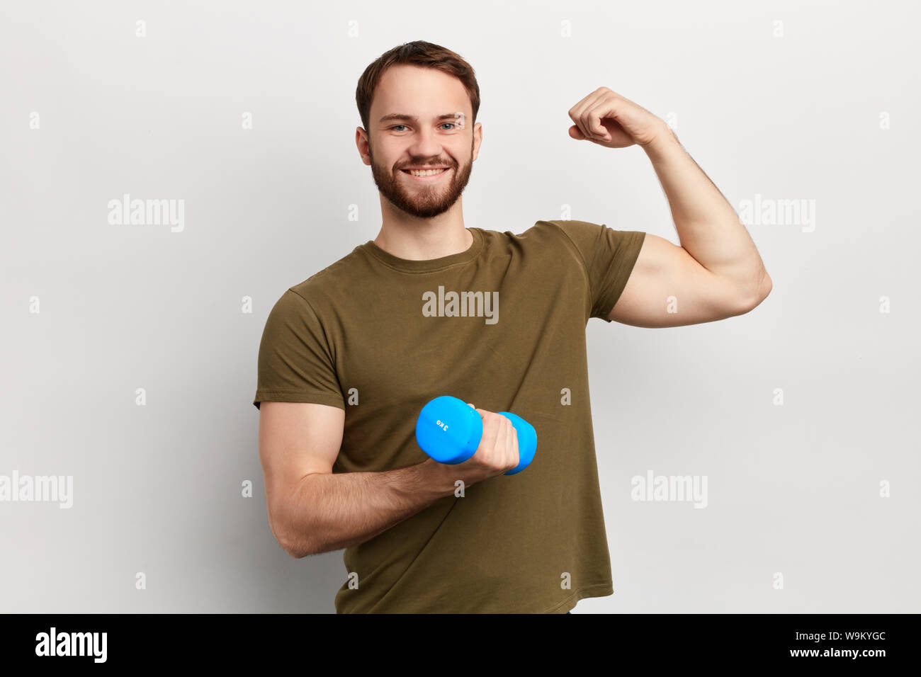 Satisfied young cheerful positive strong man lifting dumbbell isolated ...