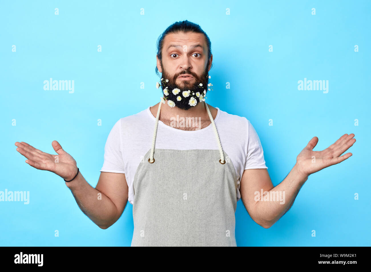 Confused young bearded man with gray apron standing and shrugging ...