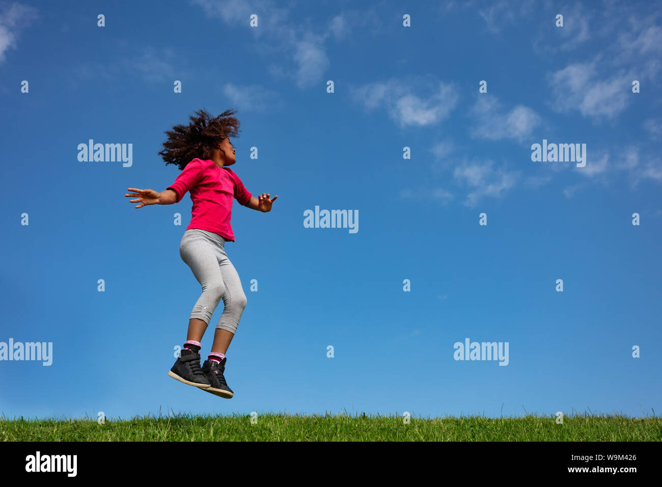 Happy curly hair girl jump over blue sky side view Stock Photo - Alamy