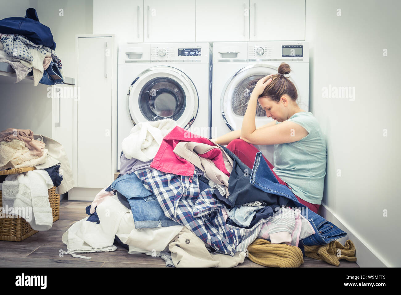 tired unhappy woman housewife in a laundry room near washing machine ...