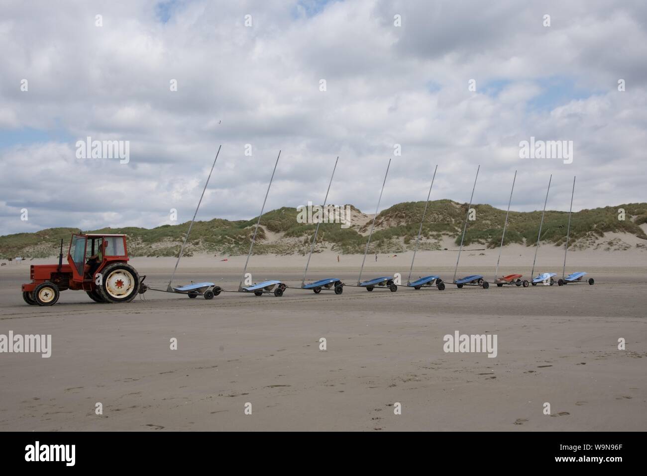 A tractor pulling 9 linked sand yachts, without sails, on to the beach ...