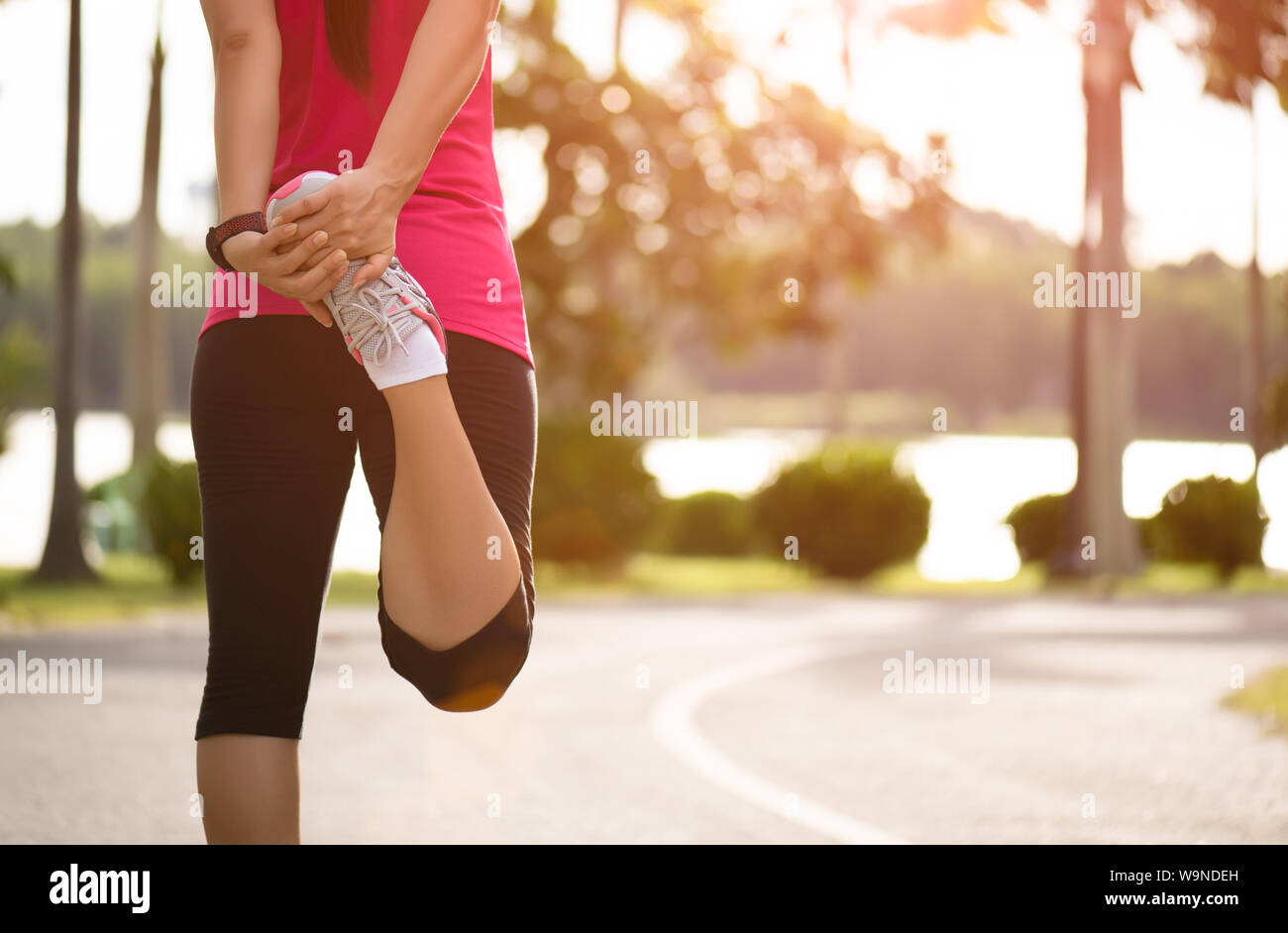 Young fitness woman runner stretching legs before run in the park. Outdoor exercise activities ...