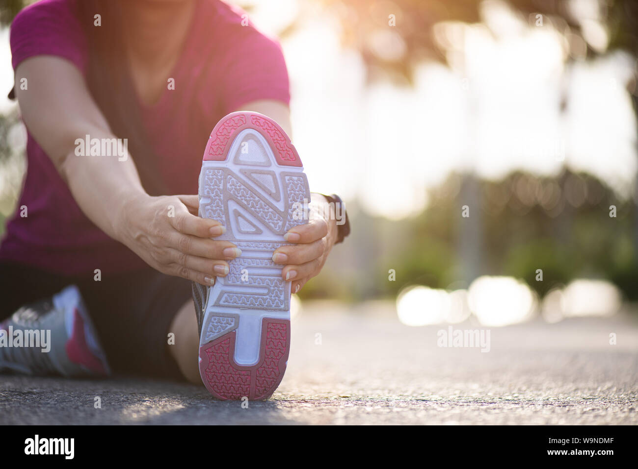 Young fitness woman runner sit on the road stretching legs before run ...